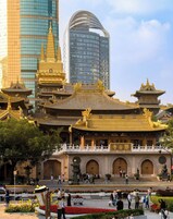 Um edifício tradicional chinês com telhados dourados elaborados e um arranha-céu moderno ao fundo.