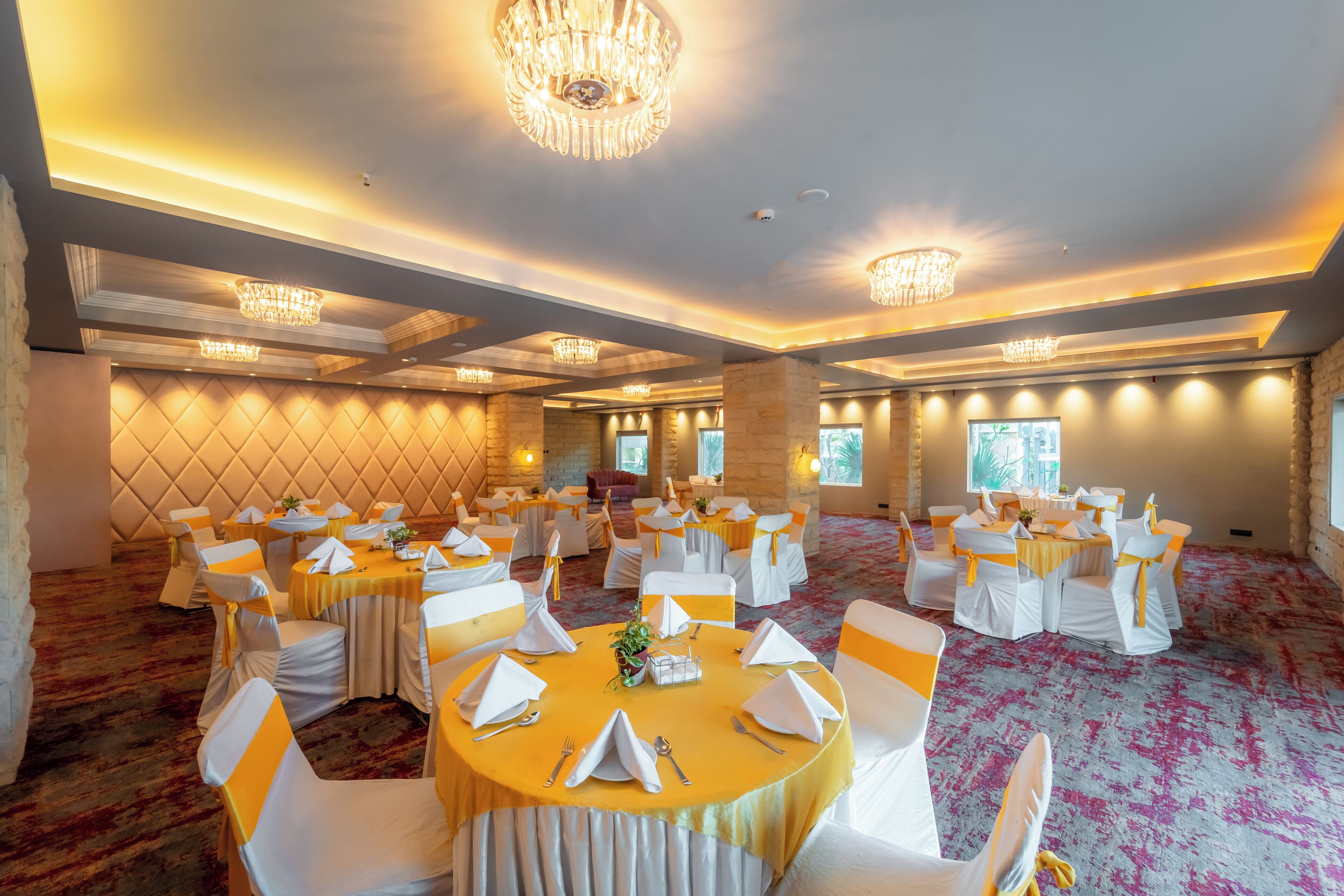 Uma sala de banquetes com mesas redondas, cadeiras brancas e lustres.