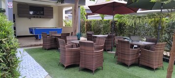 Um pátio externo com móveis de vime, mesa de bilhar e um laptop sobre uma mesa.