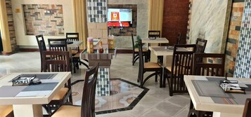 Um restaurante com várias mesas e cadeiras, uma televisão presa à parede e um chão com padrão.