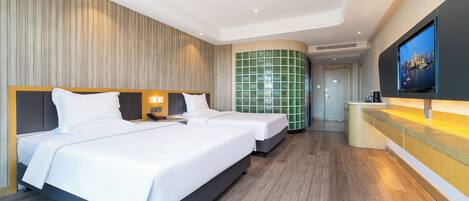 Quarto de hotel com duas camas, uma televisão, parede com azulejos verdes e chão de madeira.