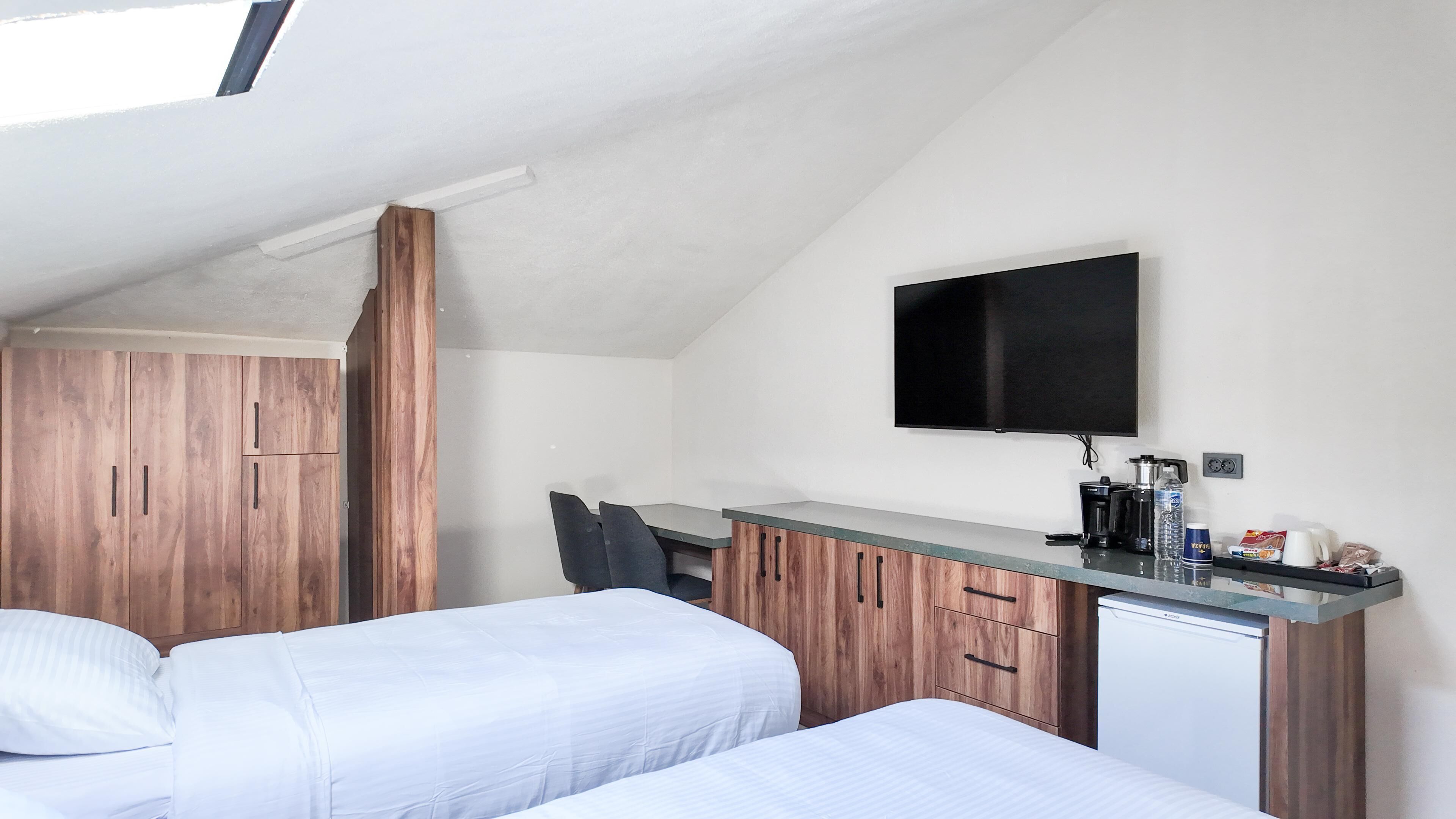 Quarto com duas camas, um guarda-roupa de madeira, uma kitchenette pequena com televisão e uma janela.