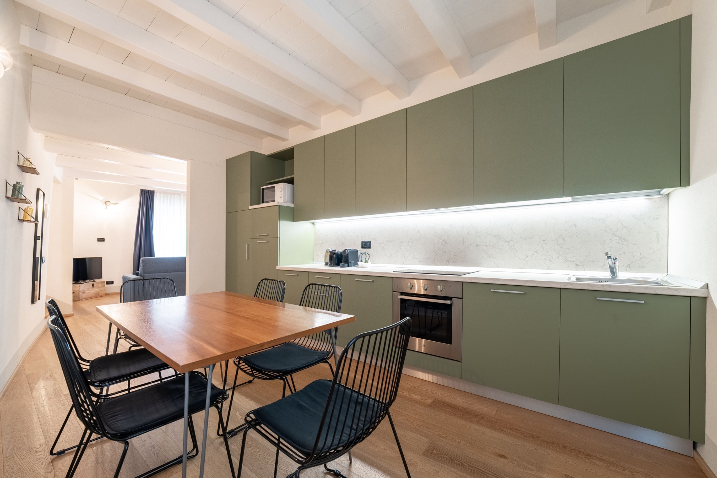 Uma cozinha moderna com uma mesa de jantar e cadeiras de madeira, armários verdes e forno embutido.