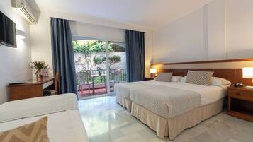 Quarto de hotel com uma cama grande, uma escrivaninha, uma cadeira, uma televisão e uma varanda com plantas.