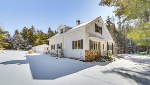 Uma casa branca com base de pedra, cercada por árvores cobertas de neve e um céu claro.