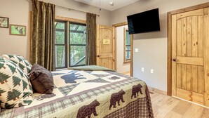 Quarto com uma cama grande, um ventilador de teto, TV fixada na parede e uma janela com cortinas.