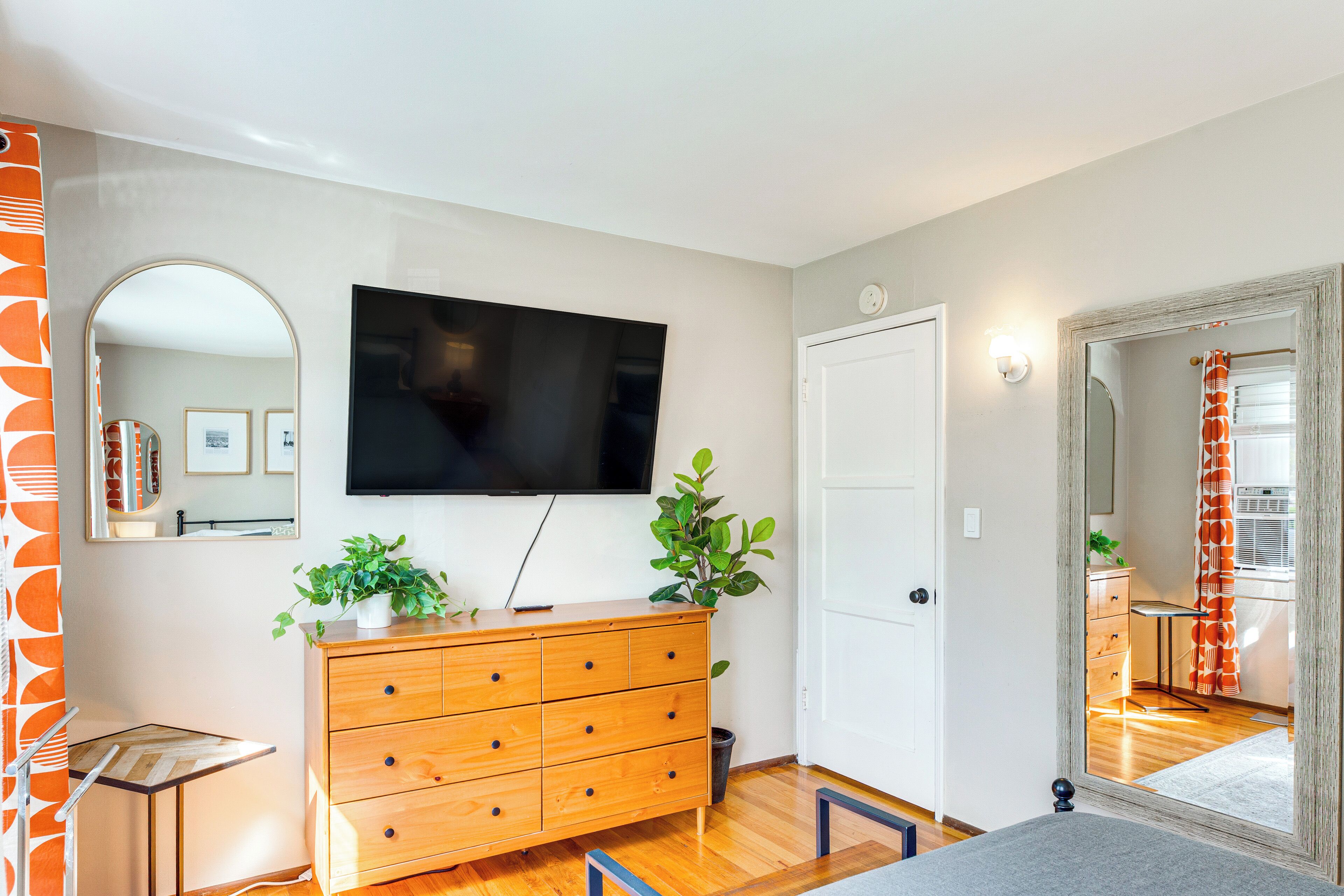 Quarto moderno com penteadeira de madeira, televisão de tela plana, espelho e porta para outro cômodo.