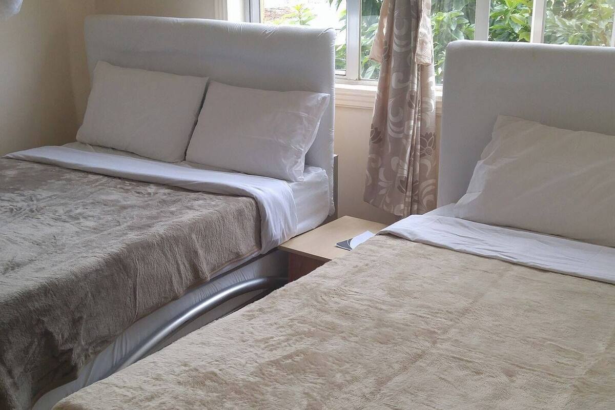 Quarto de hotel com duas camas, cada uma com cabeceira branca e manta bege.