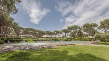 Área de piscina com espreguiçadeiras e guarda-sóis, rodeada por árvores e céu claro.
