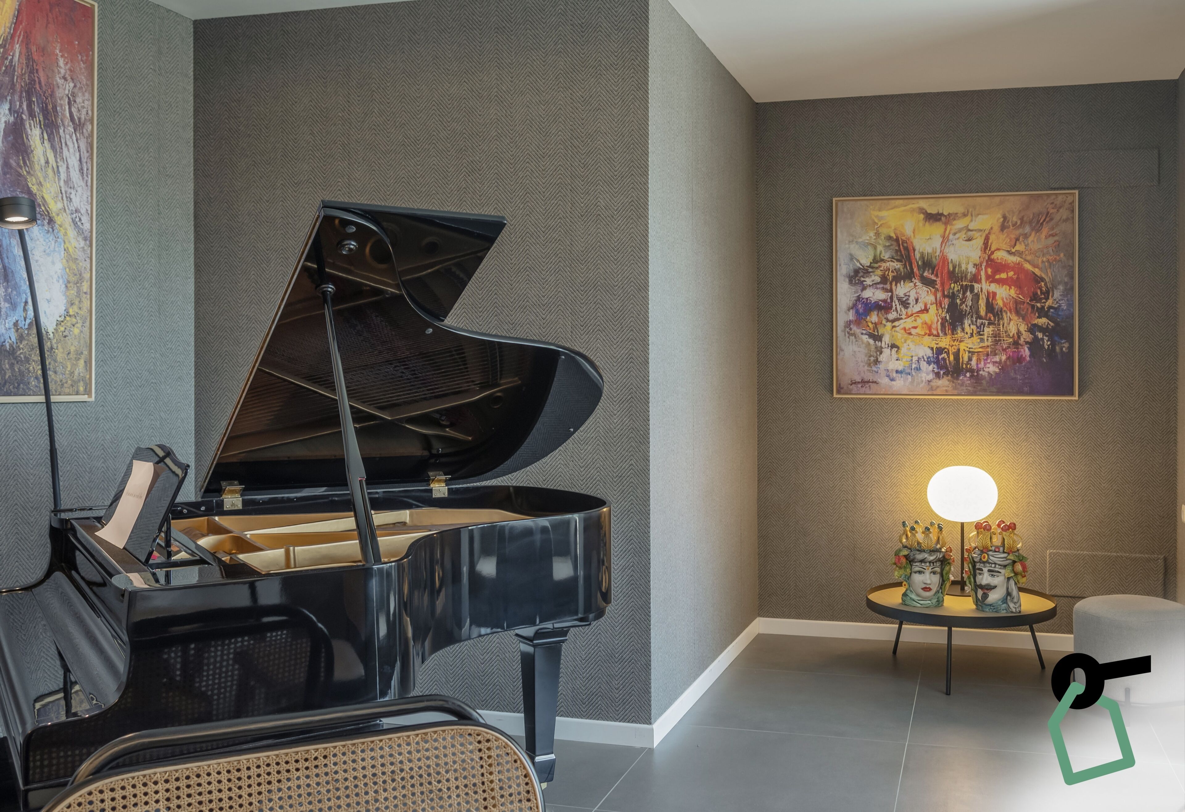 Uma sala de estar moderna com um piano de cauda, uma mesa redonda com abajur e uma grande pintura abstrata na parede.
