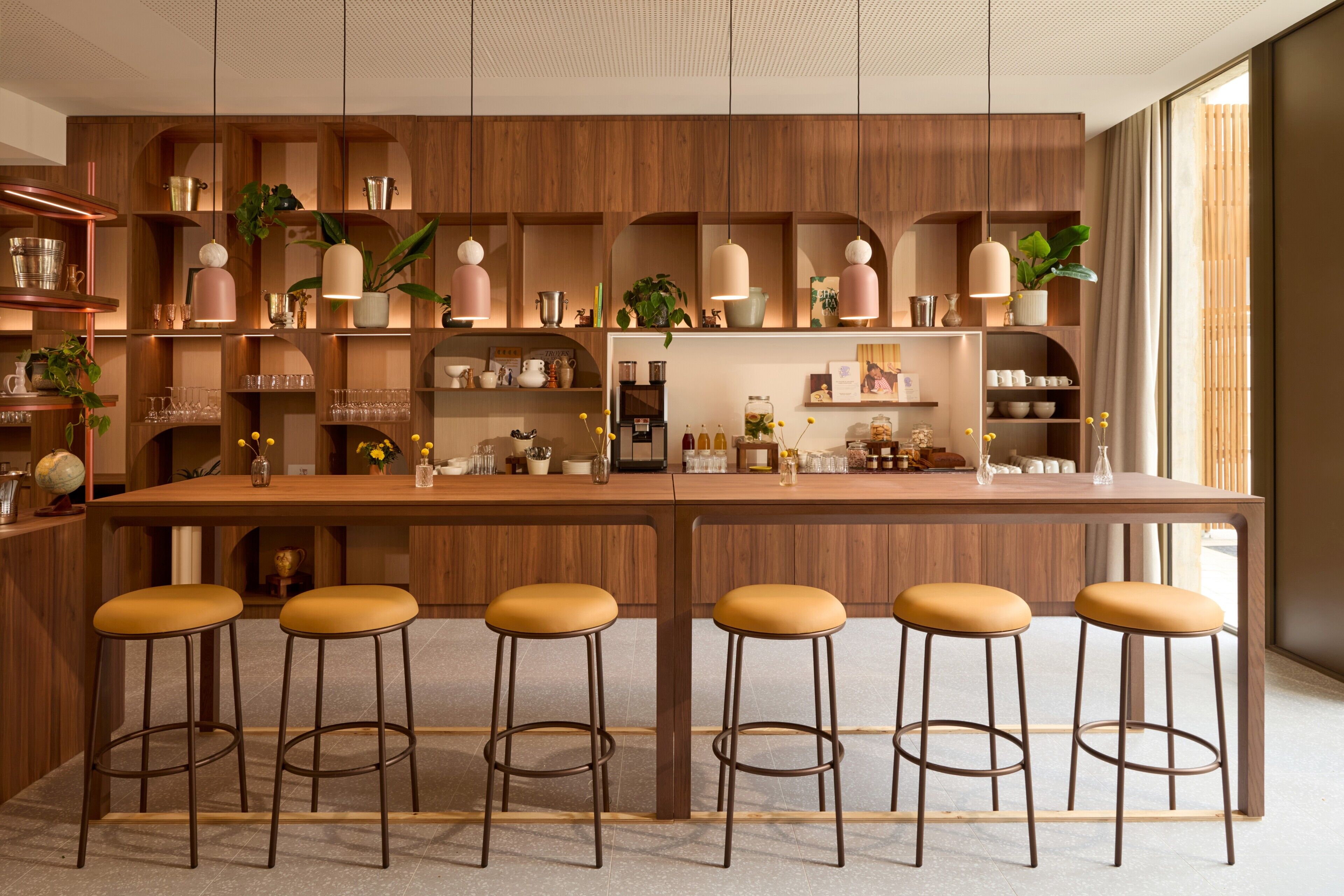 Uma cozinha moderna com armários de madeira, banquetas de bar, luminárias pendentes e diversos eletrodomésticos.