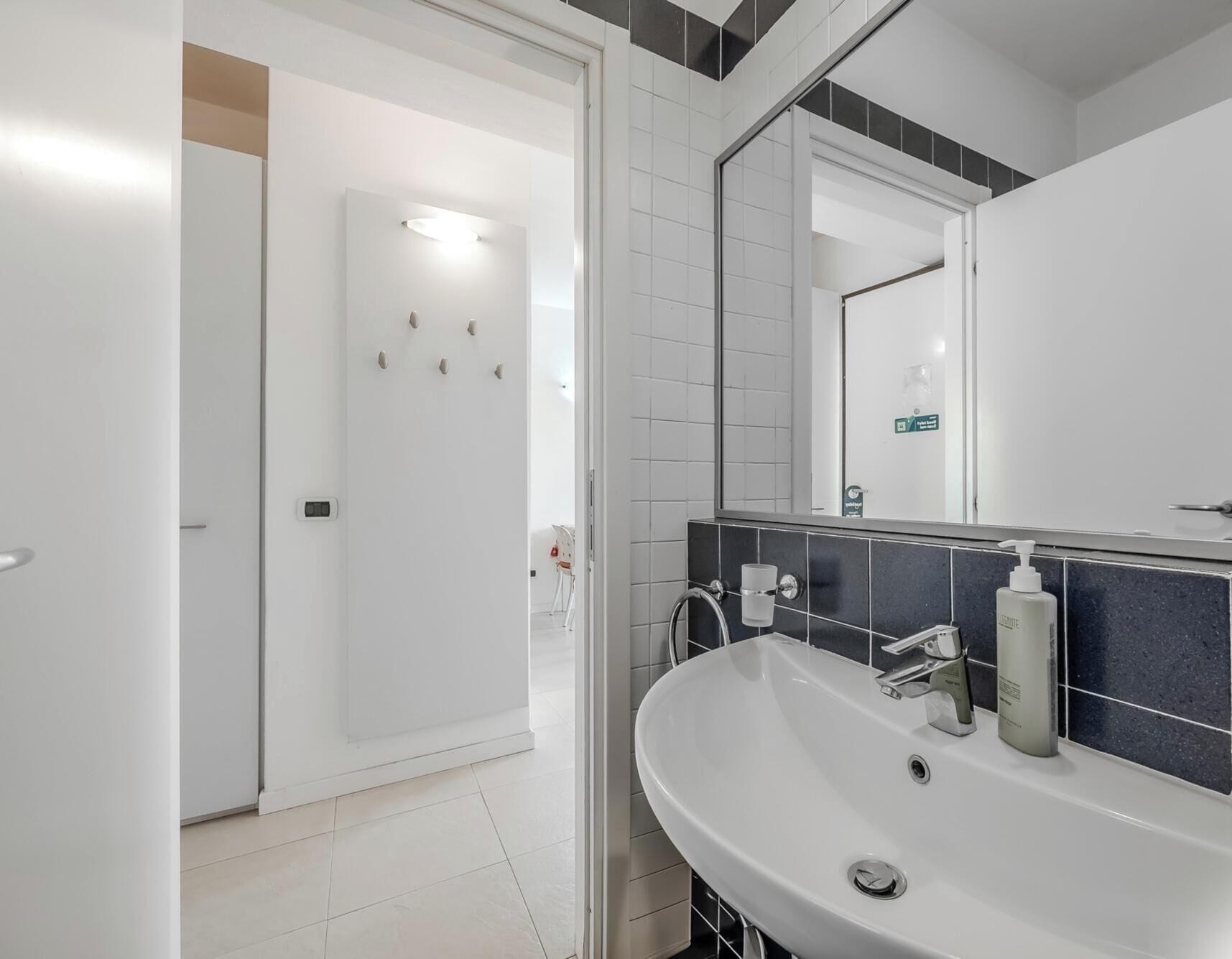 Casa de banho moderna com lavatório branco, espelho grande e zona de duche.