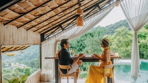 Um casal jantando à mesa com vista para uma piscina e vegetação.