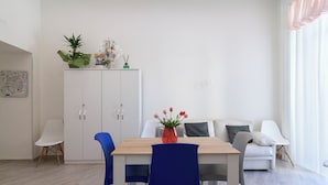 Uma sala de estar moderna com uma mesa de jantar, cadeiras azuis, um sofá branco e um aparador com objetos decorativos.