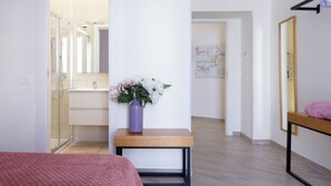 Quarto de hotel moderno com uma cama, um banco de madeira, um vaso roxo com flores, um mapa na parede e um espelho.