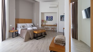 Quarto de hotel moderno com cama, escrivaninha, cadeira, televisão e janela com cortinas.