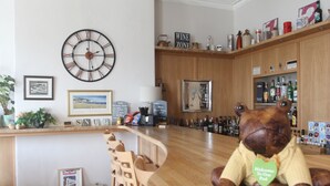 Uma área de bar com balcão de madeira, cadeiras, um relógio e uma estátua decorativa de um sapo.