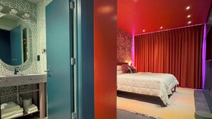 Quarto moderno com uma cama grande, banheiro com chuveiro estampado e uma parede de destaque vermelha.