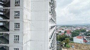 Um edifício alto com várias varandas e vista para uma área residencial ao fundo.