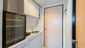 Cozinha compacta com geladeira GEA, pia e porta de madeira.