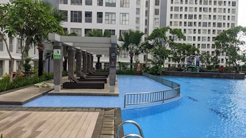 Piscina com área de deck de madeira, rodeada por vegetação e edifícios modernos.