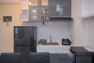 Uma cozinha compacta com geladeira preta, pia, fogão e lava-louças. Há armários sobre a pia e uma pequena área de estar com mesa e cadeiras.