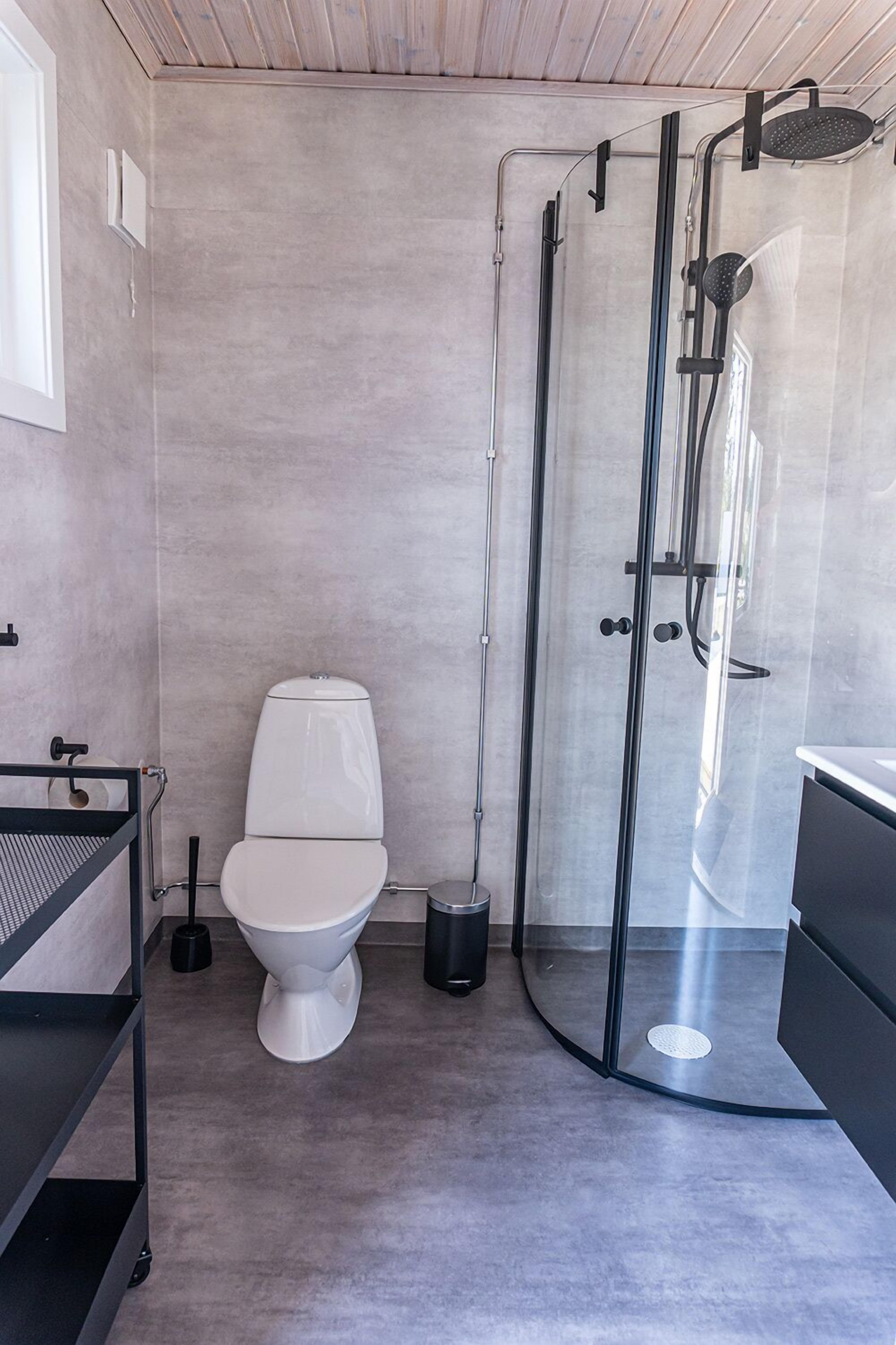 Uma casa de banho moderna com sanita, cabine de duche em vidro e lavatório preto.