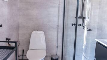 Uma casa de banho moderna com sanita, cabine de duche em vidro e lavatório preto.