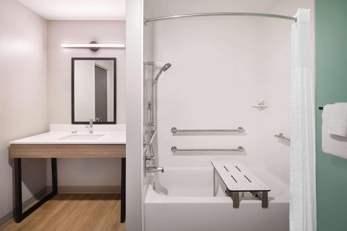 Casa de banho moderna com lavatório branco, espelho e zona de duche.