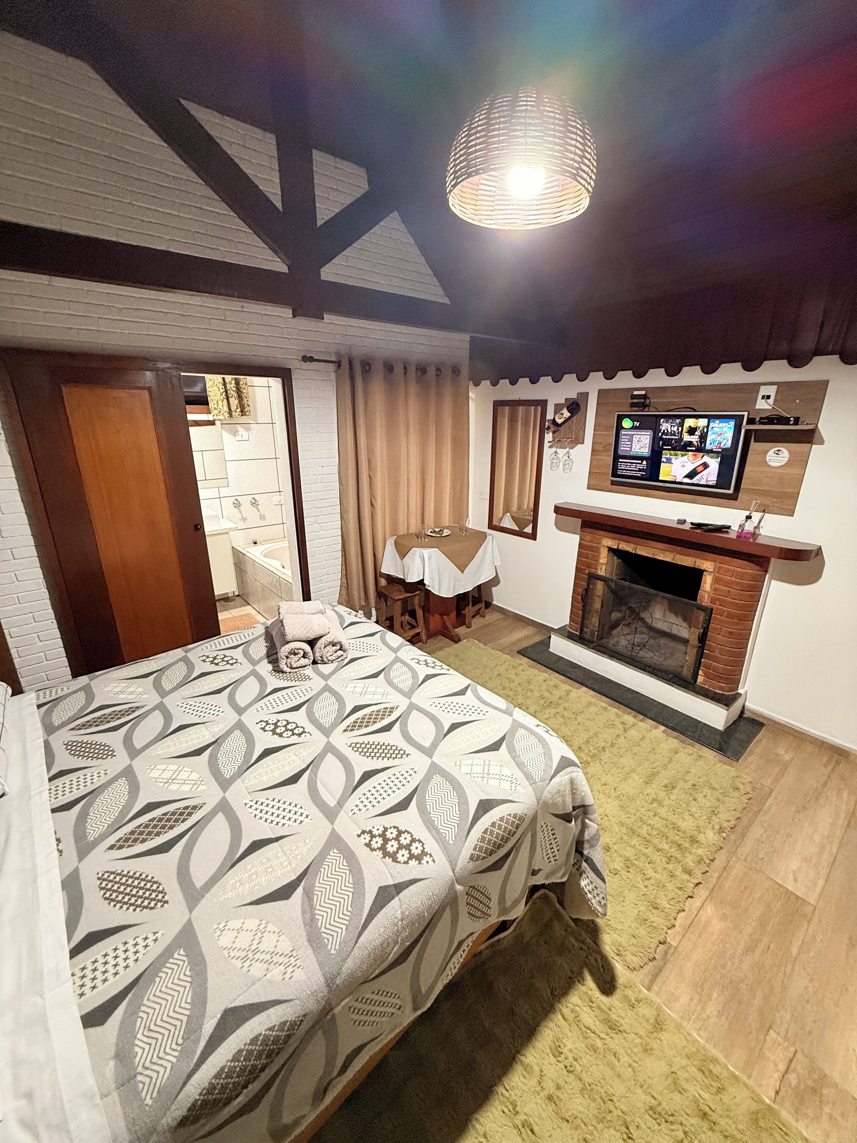 Quarto com cama, lareira, televisão e banheiro visível através de uma porta aberta.