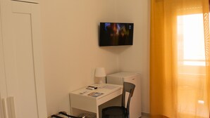 Um quarto pequeno e funcional, com escrivaninha, cadeira e televisão na parede.