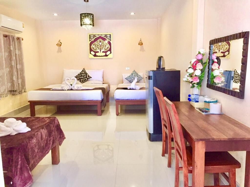Quarto de hotel com duas camas de solteiro, uma mesa de jantar de madeira, um frigorífico e um espelho com decoração floral.