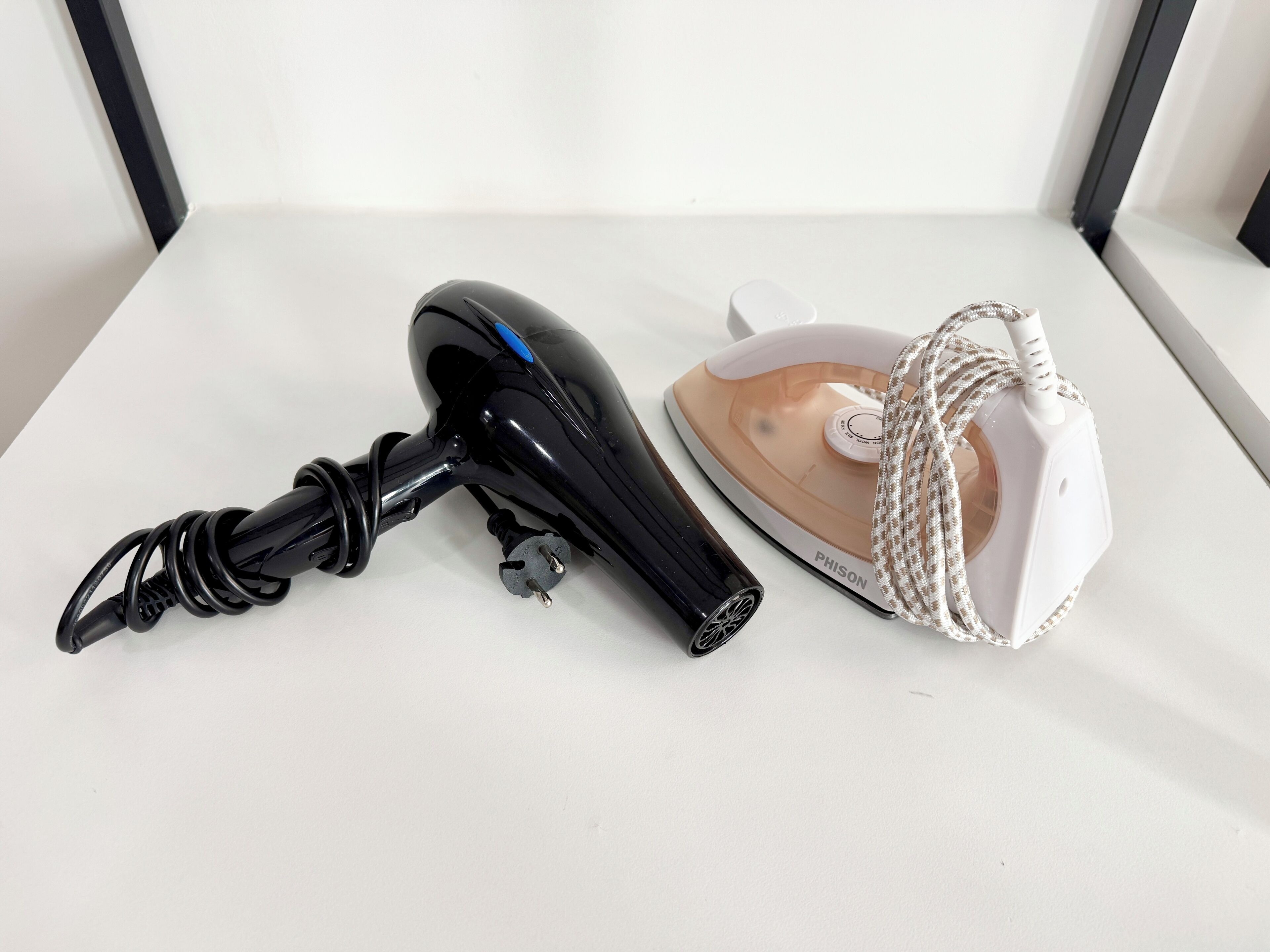 Um secador de cabelo e um ferro sobre uma superfície branca.