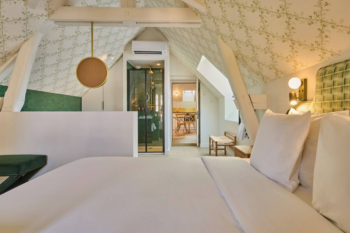 Quarto com uma cama grande, uma cadeira verde, uma mesa pequena e vista para uma sala de jantar através de uma porta de vidro.