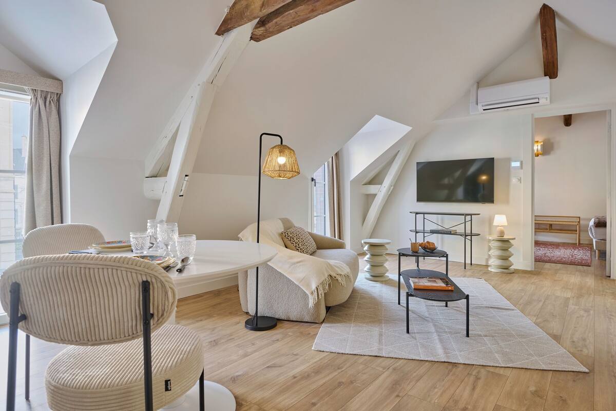 Quarto de loft moderno com teto inclinado, uma cama grande, uma mesa de jantar e uma TV na parede.