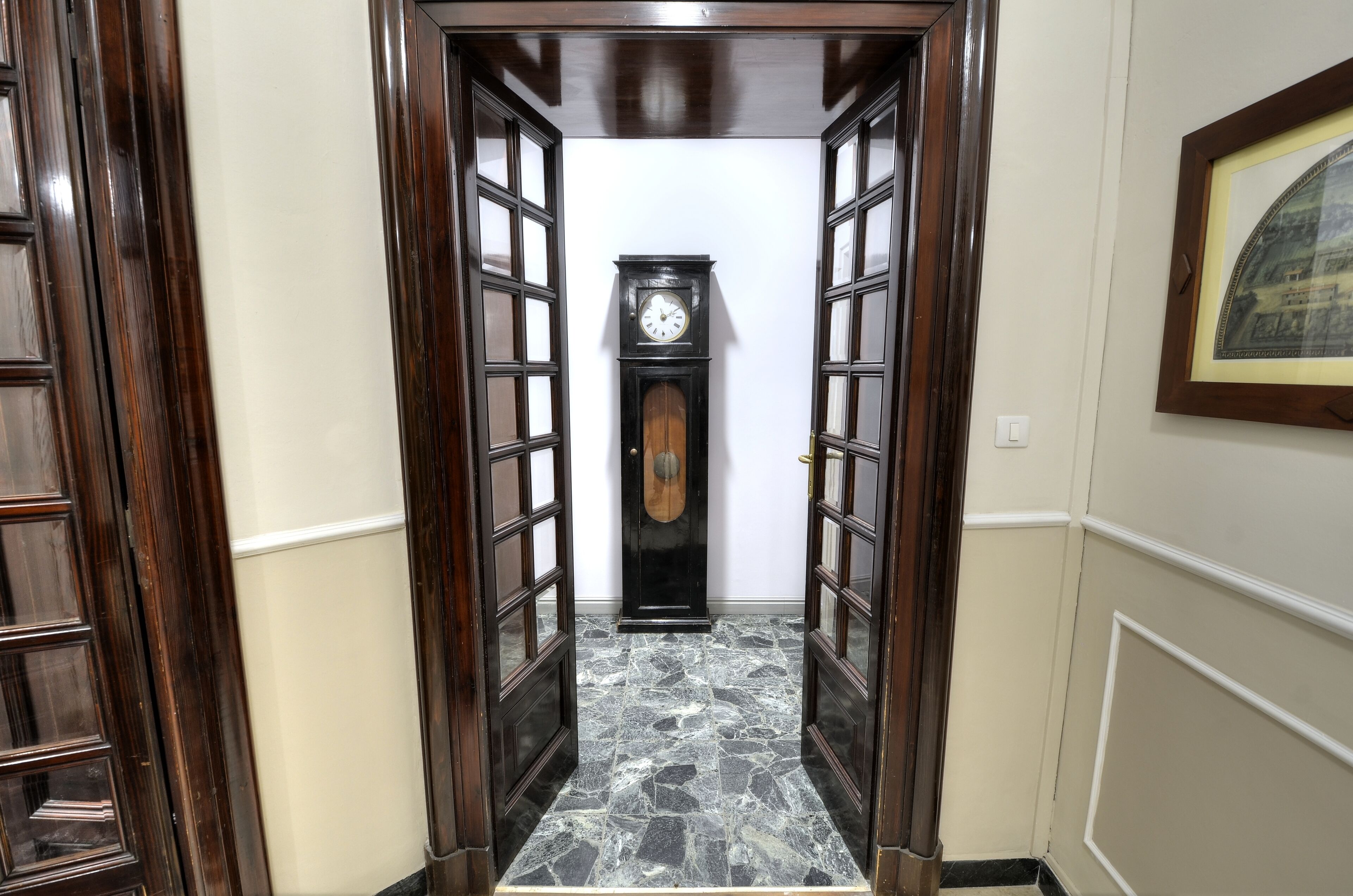 Um corredor com um porta de madeira, um relógio fixado na parede e um quadro emoldurado.