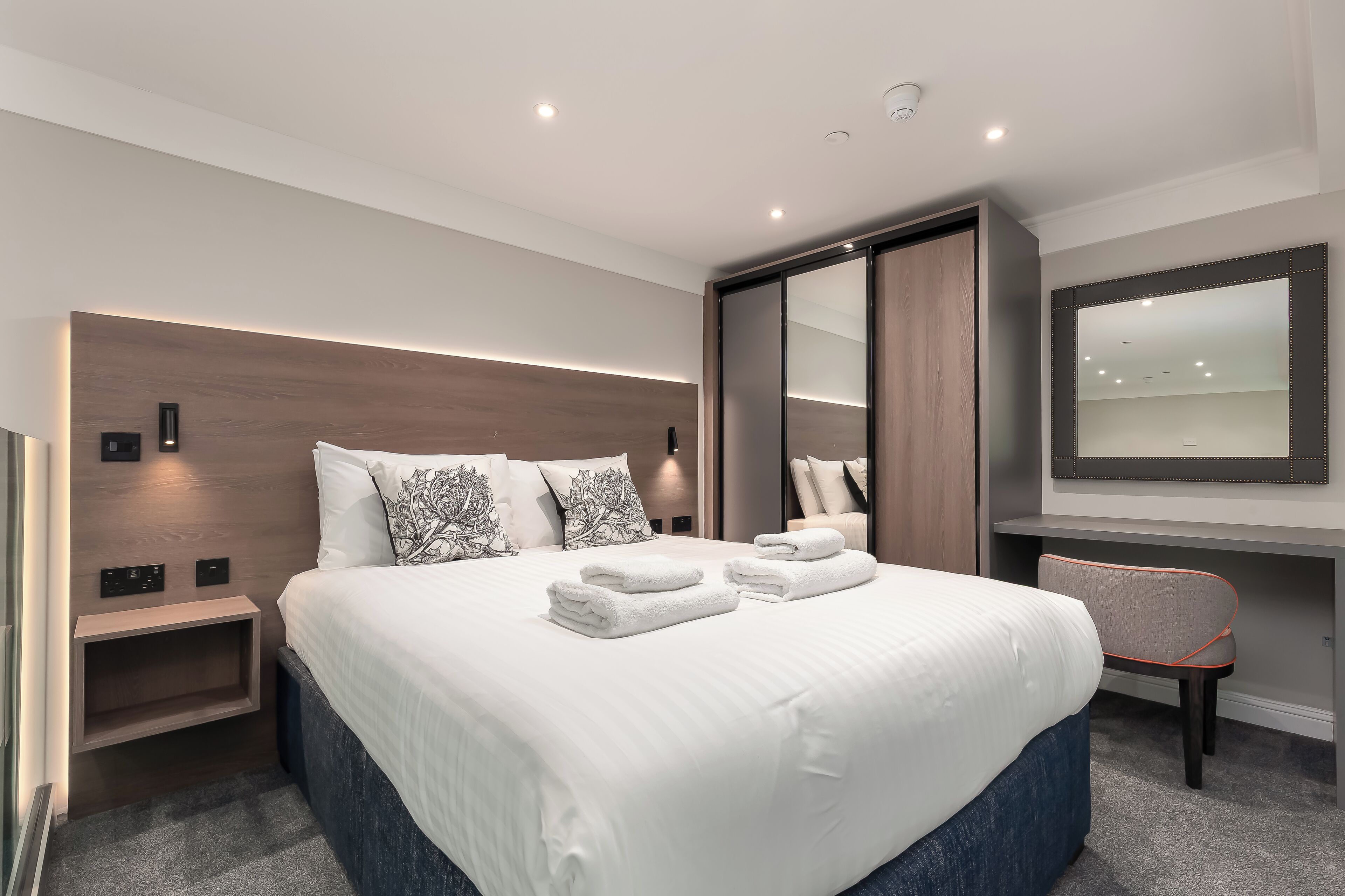 Quarto de hotel moderno com uma cama grande, mesas de cabeceira, uma escrivaninha e um espelho amplo.