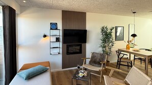 Uma sala de estar moderna com um sofá, uma mesa de jantar, cadeiras, uma televisão e uma planta.