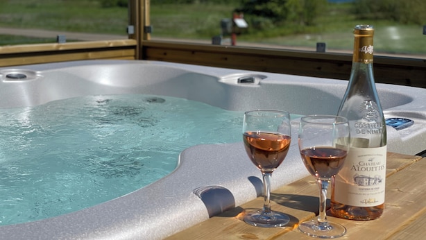 Uma banheira de hidromassagem com duas taças de vinho e uma garrafa de vinho sobre uma mesa de madeira.