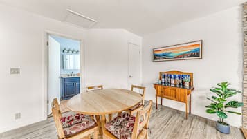 Uma área de refeições com mesa e cadeiras de madeira, cozinha ao fundo e um quadro na parede.