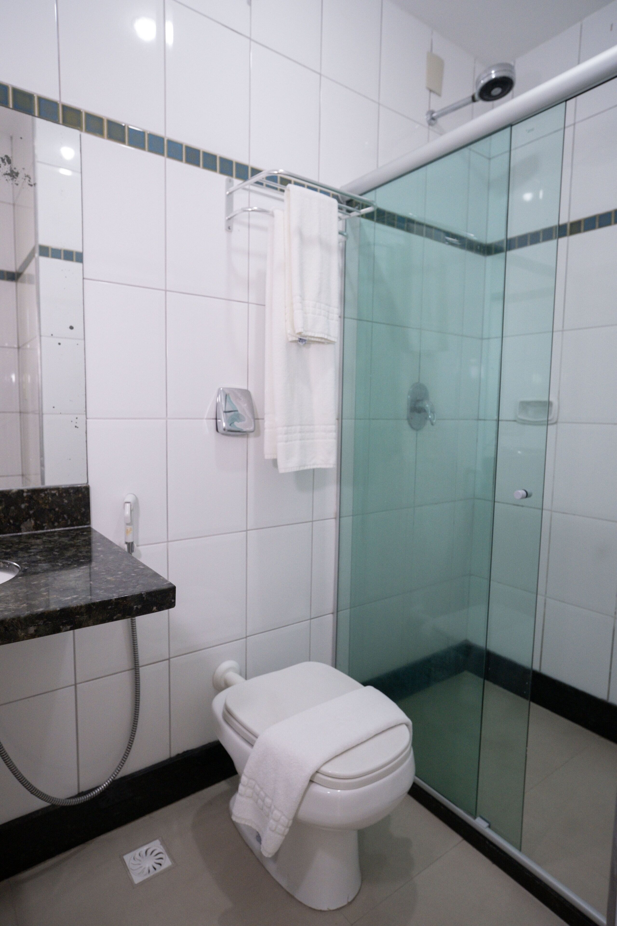 Casa de banho com chuveiro em cabine de vidro, sanita branca e bancada de mármore com dispensador de sabonete.