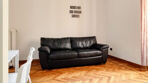 Um sofá de couro preto em um quarto com piso de assoalho de madeira e um radiador branco.