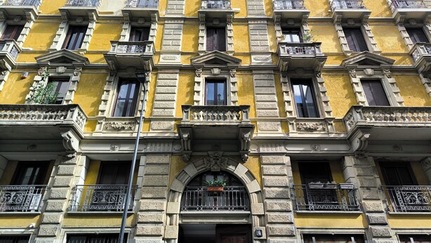 Um edifício de vários andares com fachada amarela, varandas elaboradas e uma entrada central com arco decorativo.