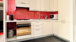 Uma cozinha moderna com armários brancos, painel de parede vermelho, eletrodomésticos de aço inoxidável e piso de madeira.