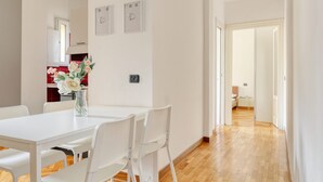 Cozinha moderna com armários brancos, painel de fundo vermelho e uma área de jantar com mesa e cadeiras brancas.