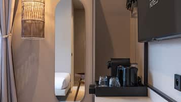 Quarto de hotel moderno com cama, escrivaninha com cafeteira, espelho e luminária pendente.