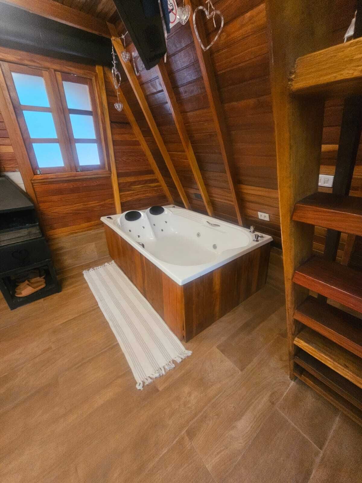Uma cabana de madeira com hidromassagem, prateleiras de madeira e uma janela.