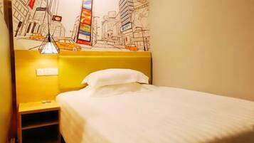 Quarto de hotel com cama, mesa de cabeceira, luminária e um mural na parede retratando um horizonte urbano.