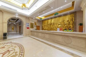 Área de recepção de hotel com piso de mármore, balcão de atendimento e uma grande estátua dourada.