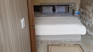 Um quarto com um arco de pedra, uma cama com roupa de cama estampada, uma mesa de cabeceira com um vaso e um guarda-roupa de madeira.